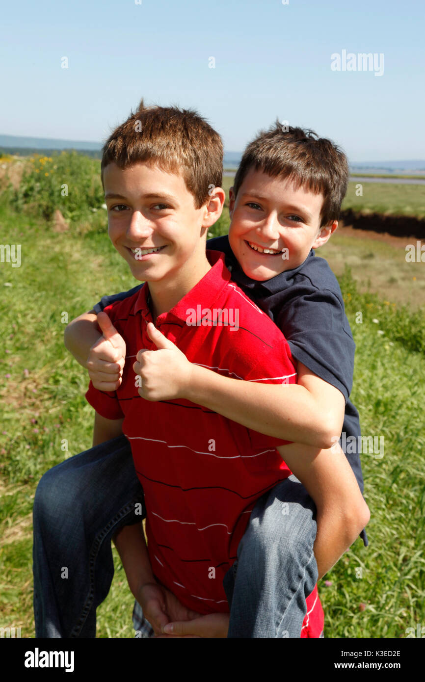 two brothers play outside piggy back thumbs up Stock Photo - Alamy
