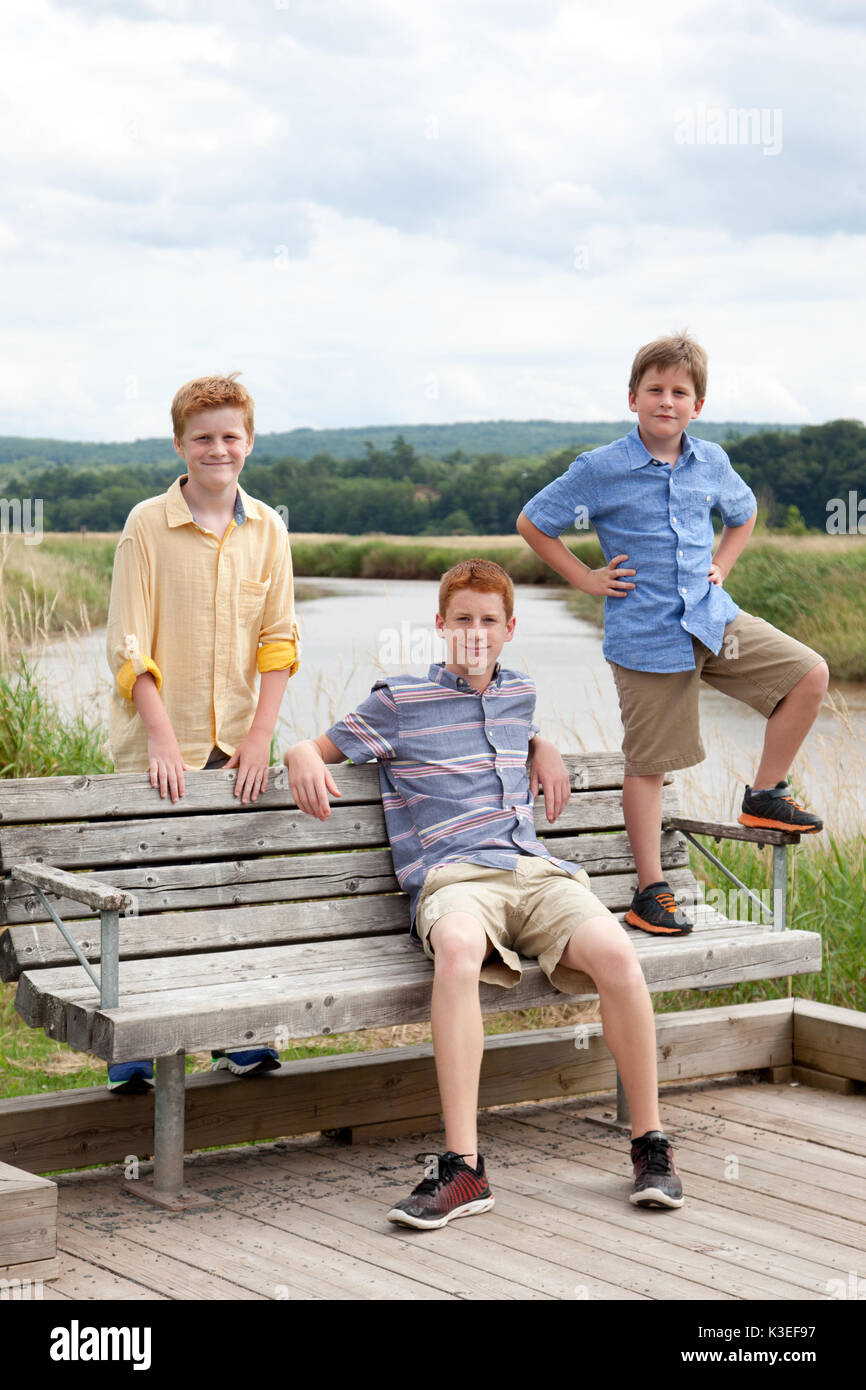 Three brothers next to and on a wooden bench outdoors by a river Stock ...