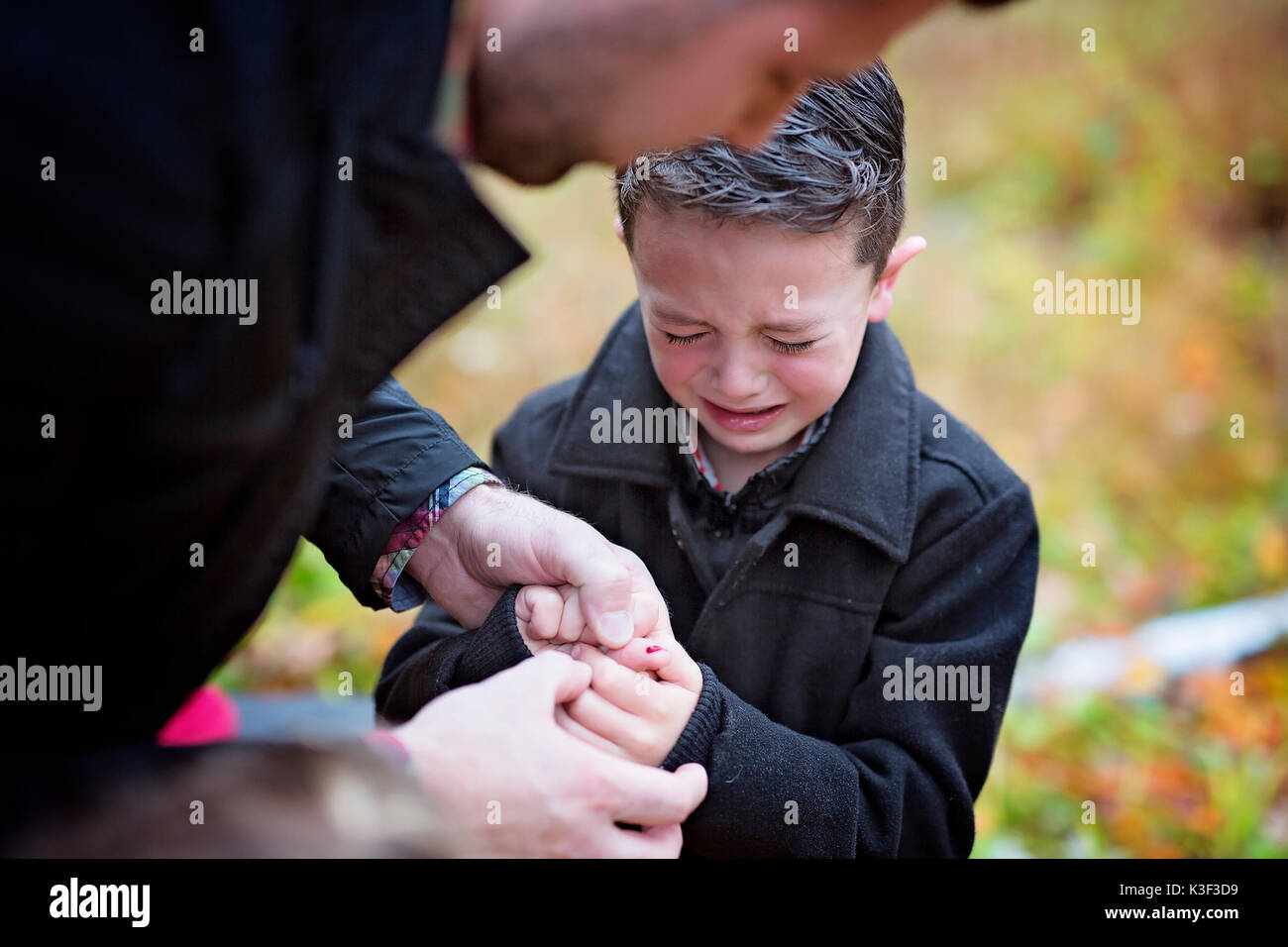 Small boy crying in pain injuring his hand. Father provides first aid ...