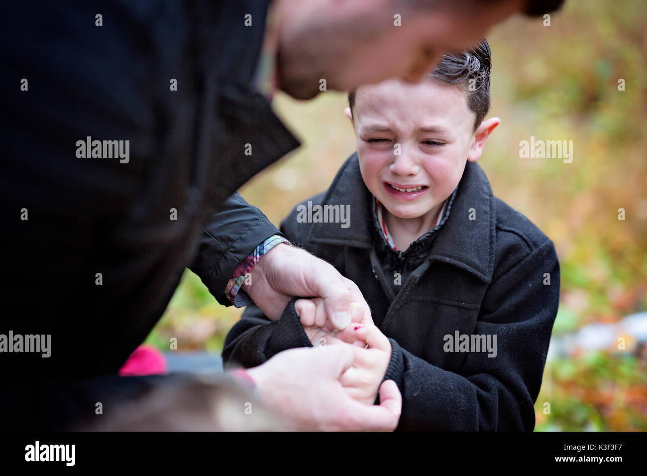 Small boy crying in pain injuring his hand. Father provides first aid ...