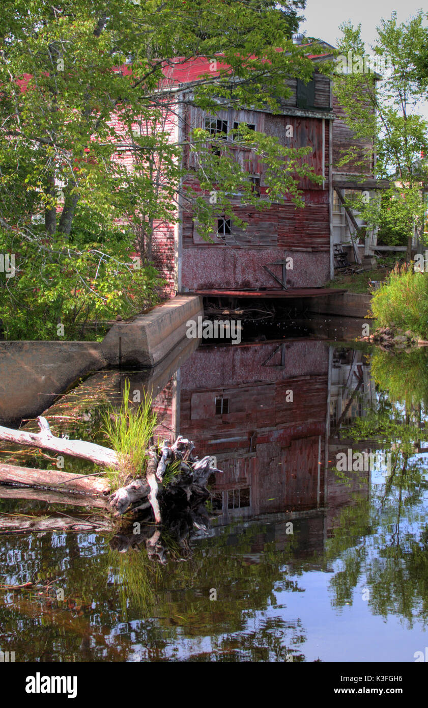 a red barn beside a dam with river flowing and building reflected in ...