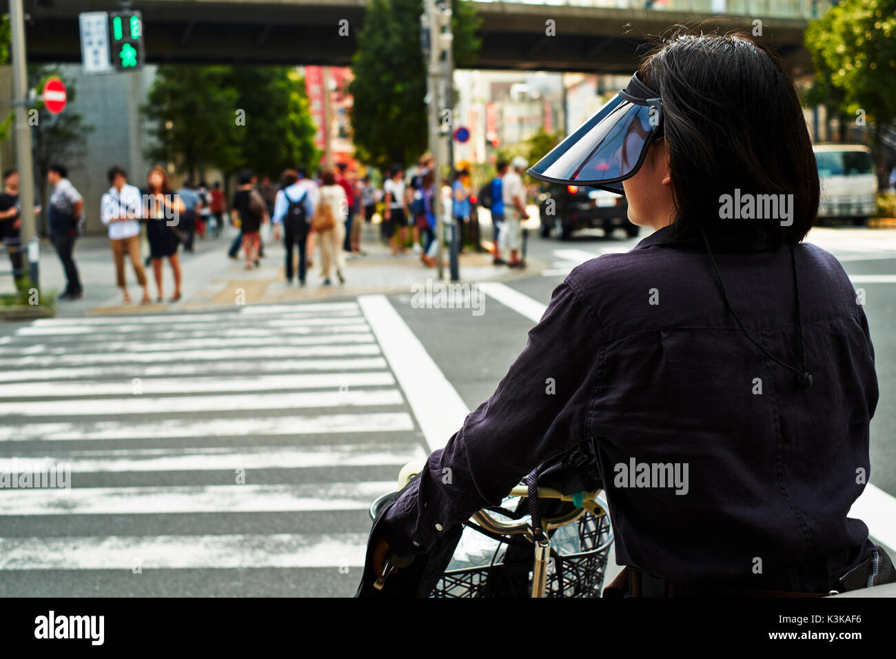 Japanese woman in black and sun visor standing with bicycle at zebras ...