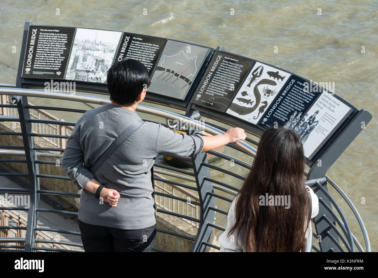 A young woman on London Bridge reading a noticeboard about the history ...