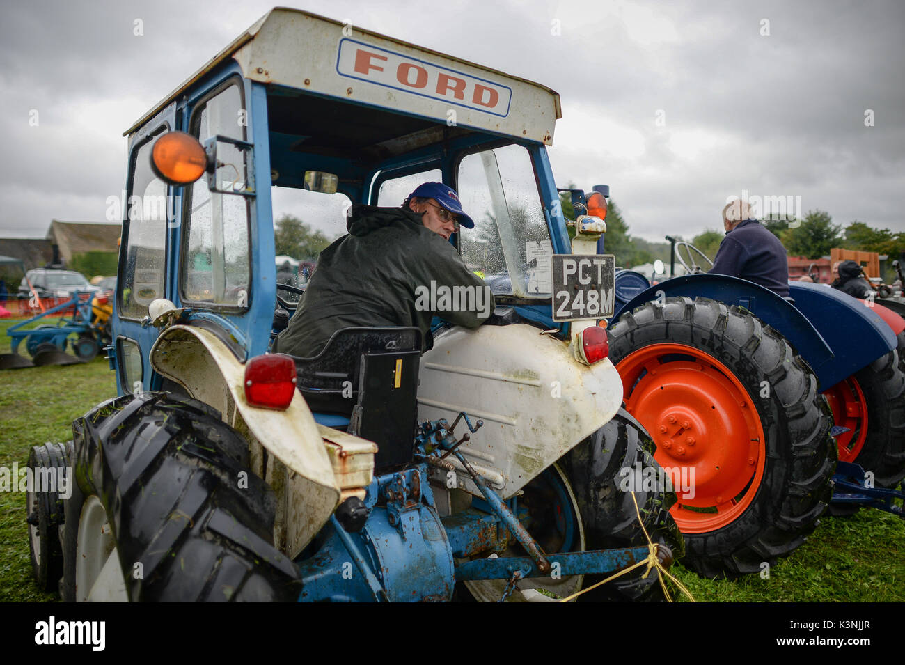 A tractor enthusiast relaxes in his covered cab aboard his vintage Ford ...