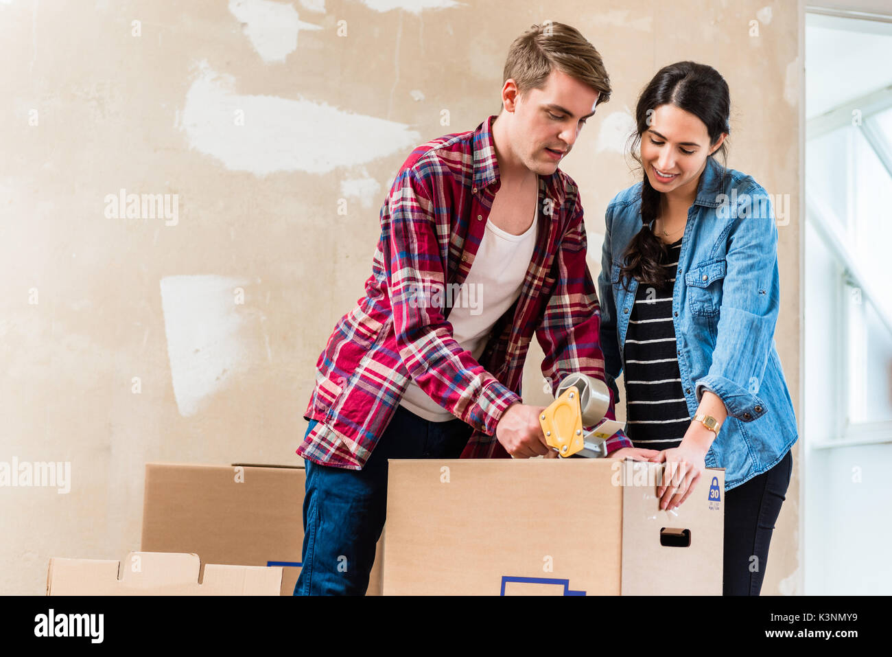 Young man and his girlfriend sealing a box while renovating thei Stock ...