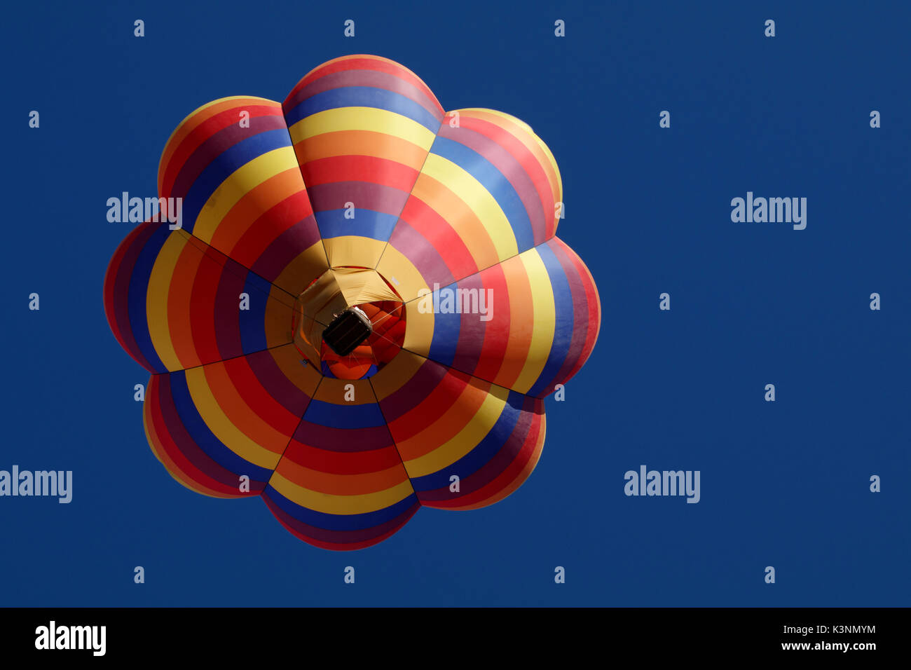 A rainbow colored hot air balloon floats directly overhead in the blue ...