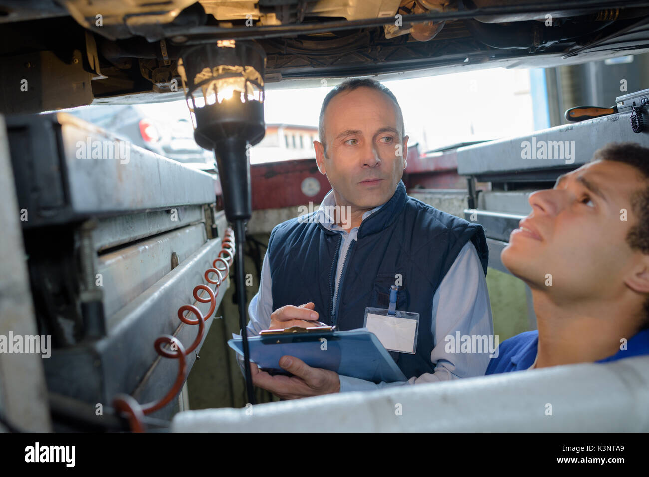 mechanic and trainee working under car Stock Photo - Alamy