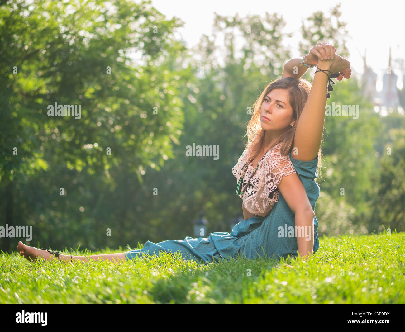 Portrait of young white woman runner stretching legs in the park. Green ...