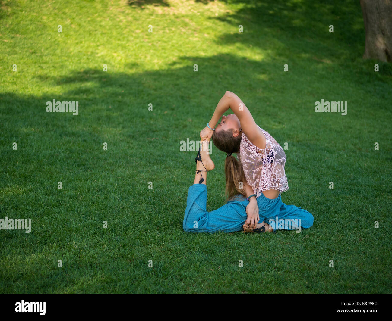 Portrait of young white woman runner stretching legs in the park. Green ...