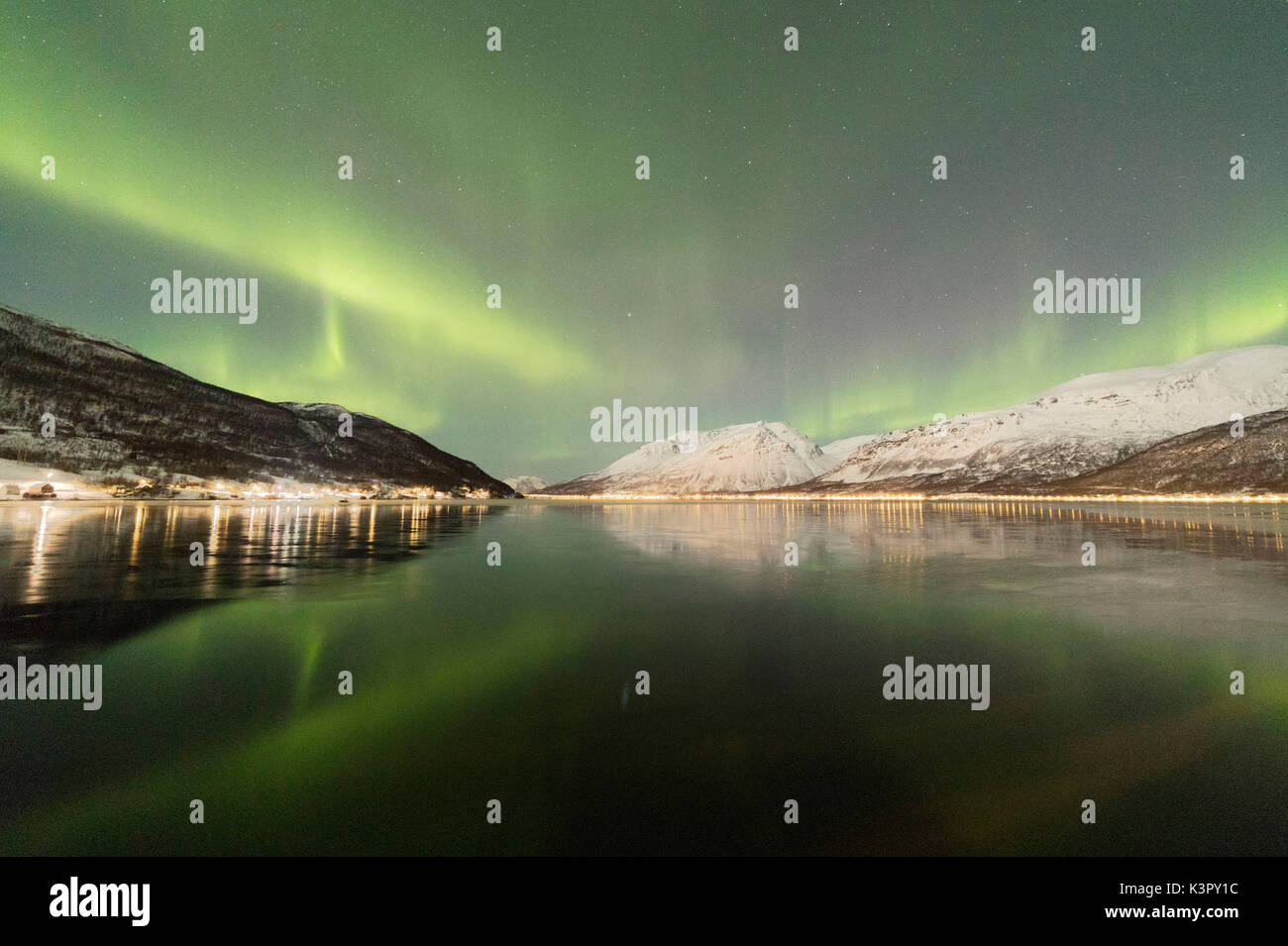 The Northern Lights is reflected in the icy sea surrounded by snowy ...