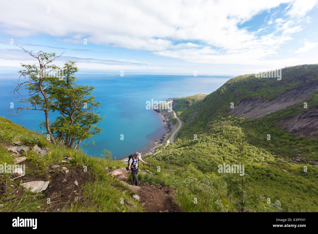 Hiker on path surrounded by woods and turquoise water of the Norwegian ...