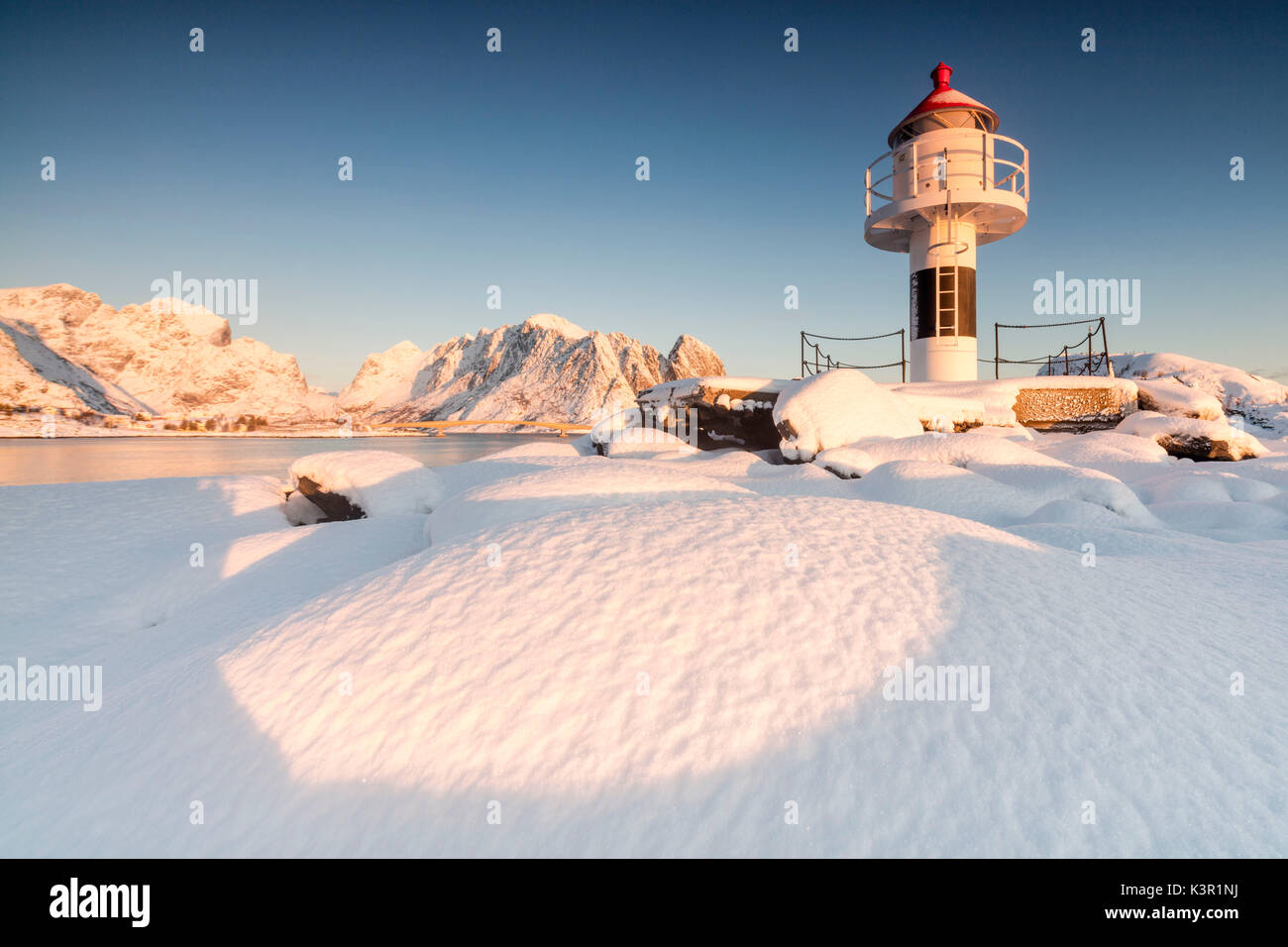 The lighthouse surrounded by snow frames the snowy peaks and the frozen ...