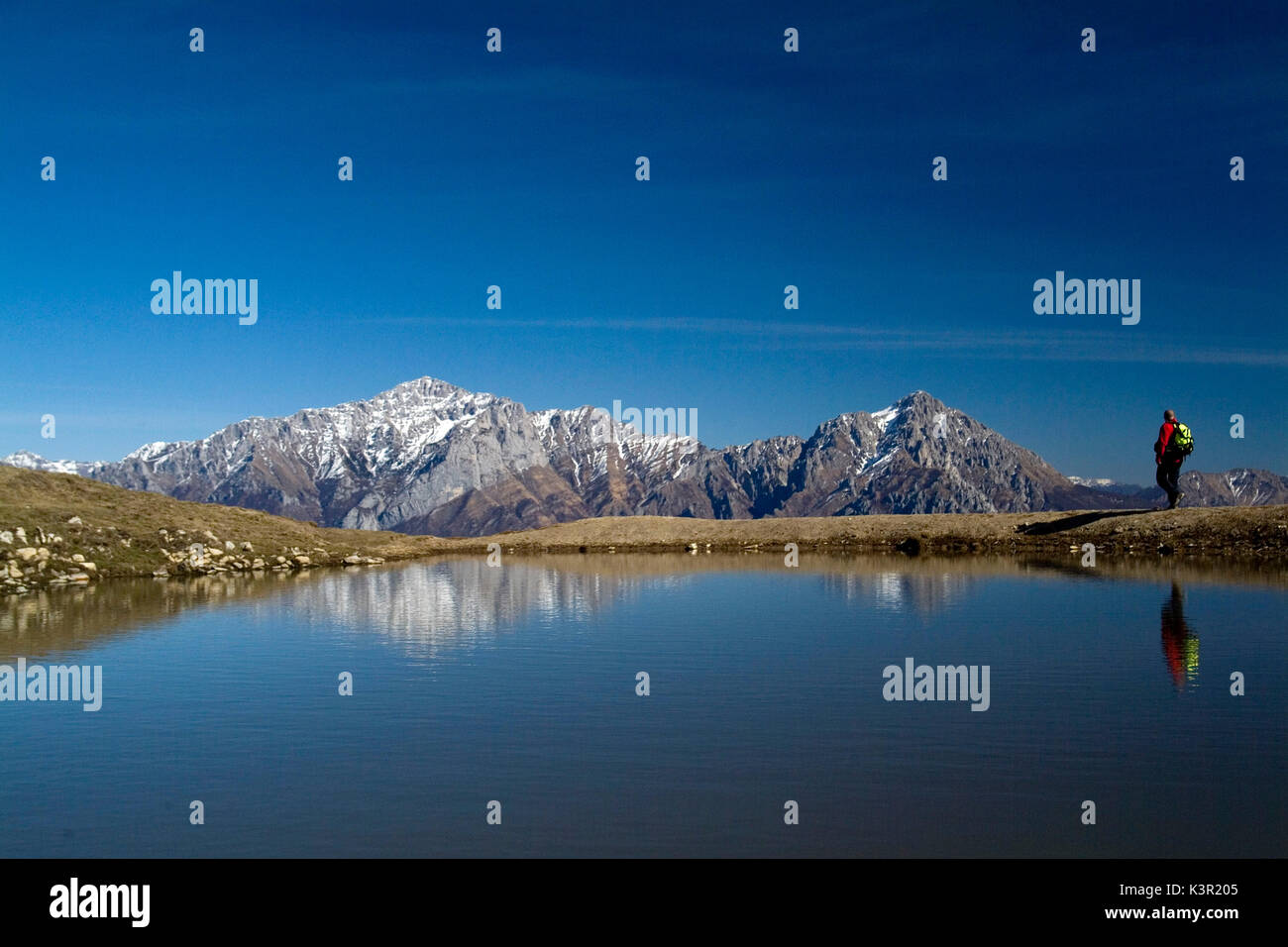 A hiker along the ridge of Mount San Primo reflected in a seasonal pond ...