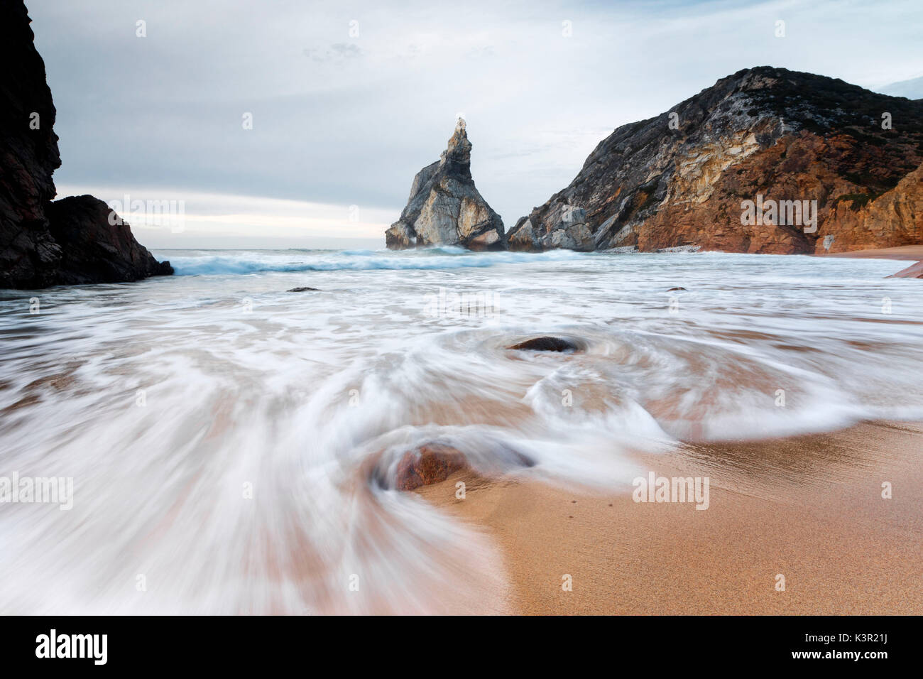 Ocean waves crashing on the sandy beach of Praia da Ursa surrounded by ...