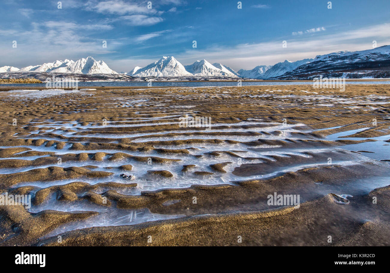 The icy sandy beach surrounding the snow capped mountains Breivikeidet ...