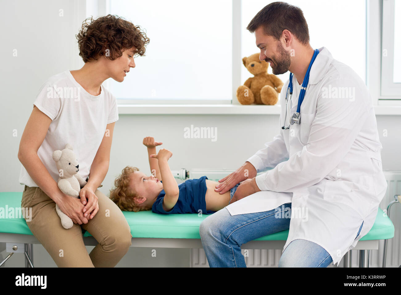 Portrait of smiling doctor examining stomach of little boy and asking ...