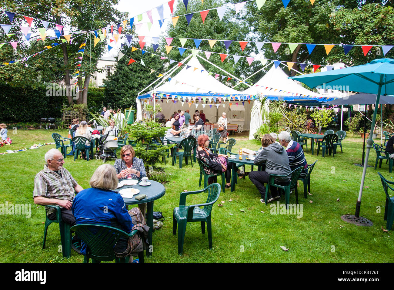 People having tea on the lawn. Several groups sitting at tables with ...