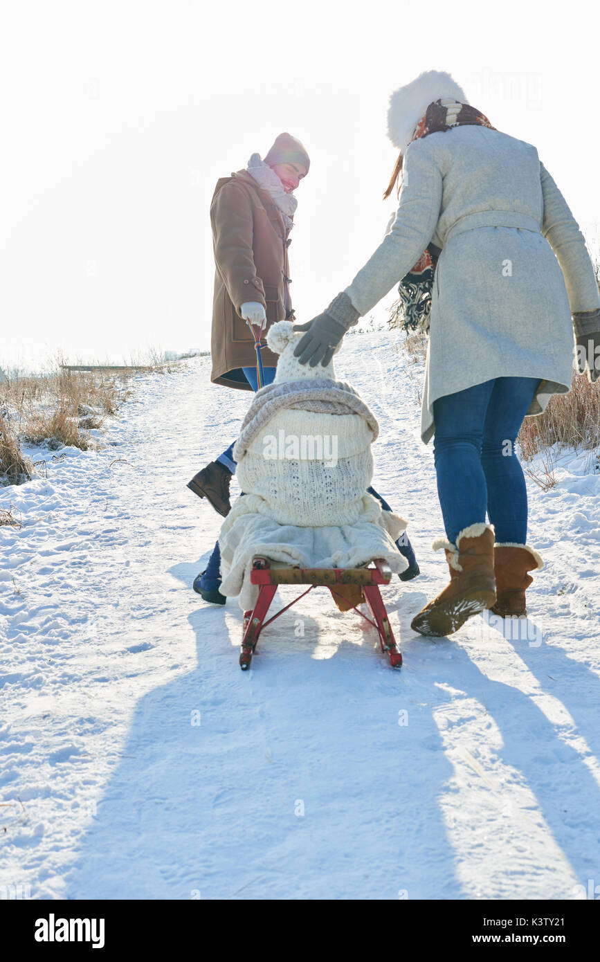 Parents pull child in winter toboggan walk in the snow Stock Photo - Alamy