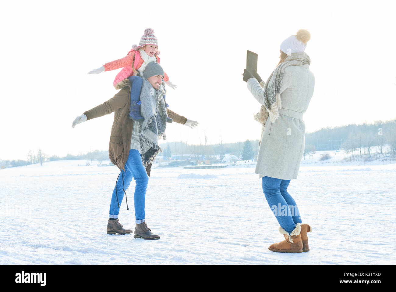 Family having fun in winter while mom takes photograph of piggyback ...