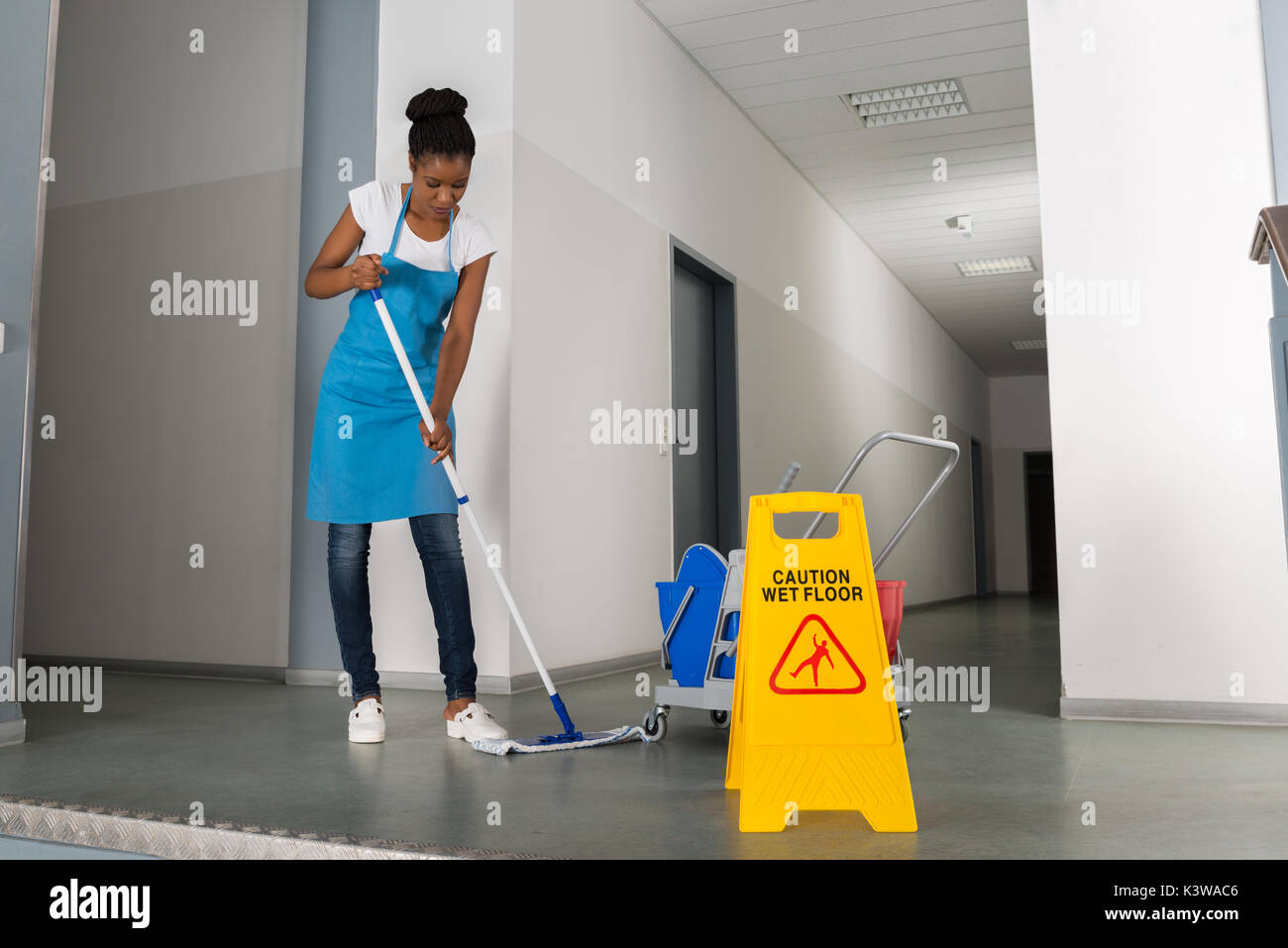 African Woman Mopping Corridor Besides Caution Sign Stock Photo - Alamy