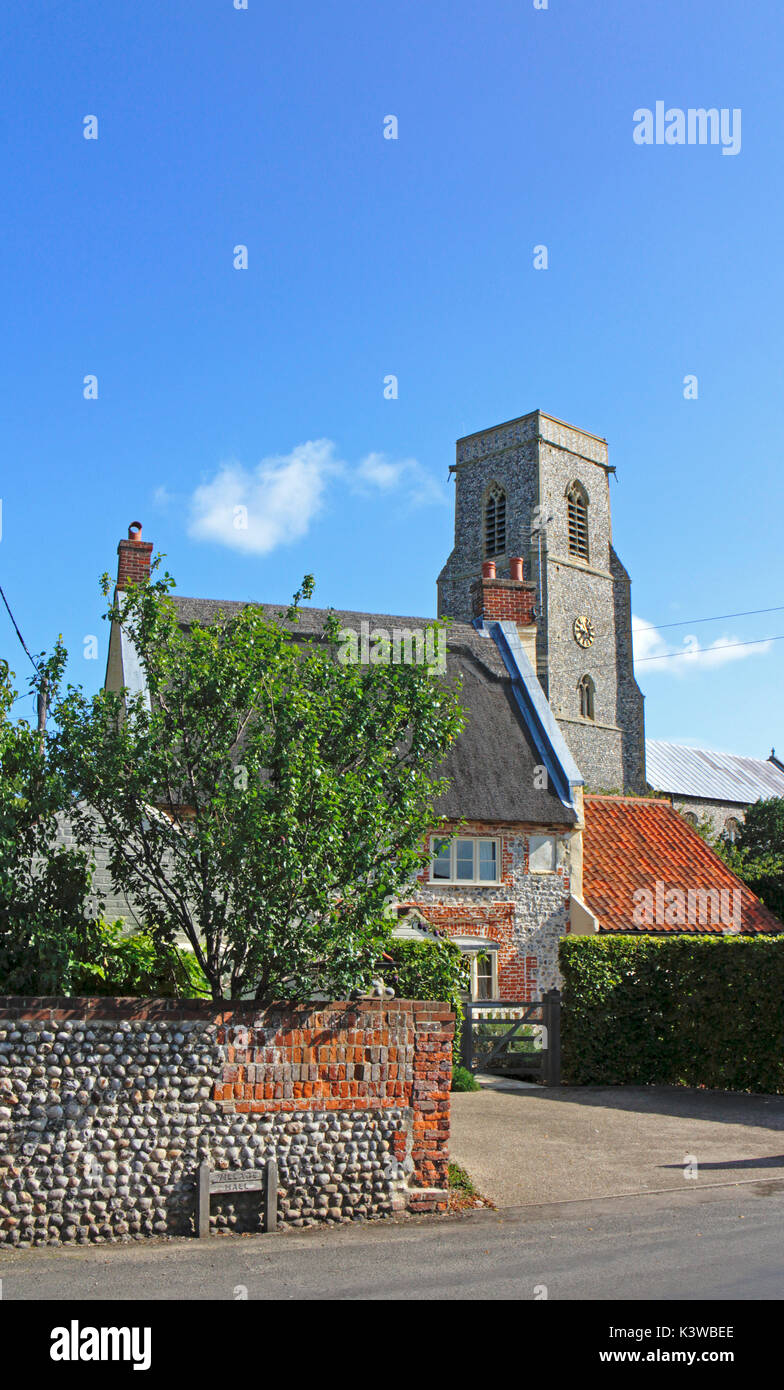 A view of a traditional thatched Norfolk cottage with parish church at ...