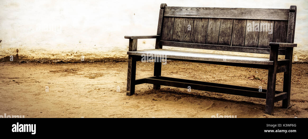 A lone bench sitting on dirt with a white wall behind Stock Photo - Alamy