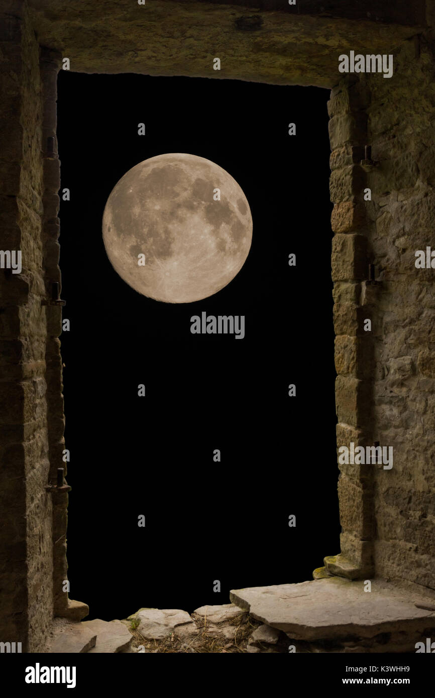 Full moon on the dark sky visible through old ancient stone window ...
