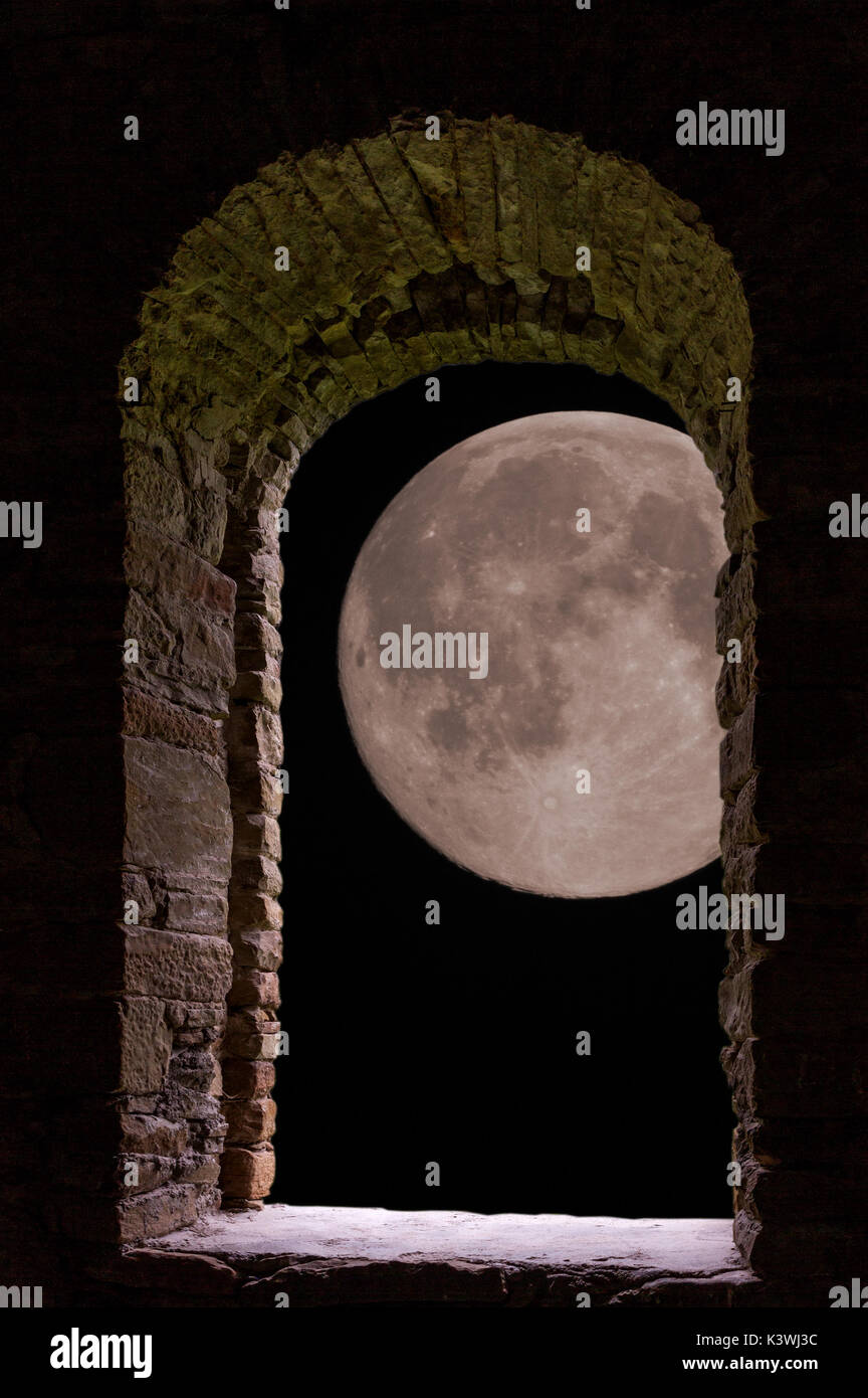 Full moon on the dark sky visible through old ancient stone window ...
