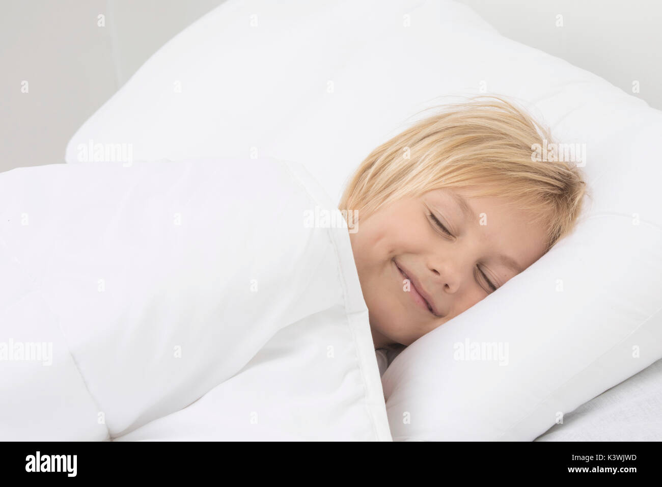 Lovely little boy peacefully sleeping in a bed smiling seeing a dream ...