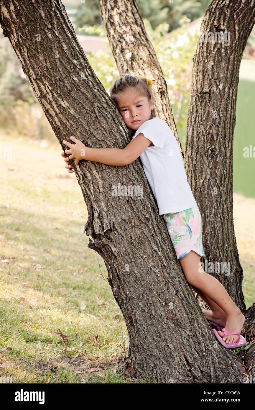 Sad little girl hugging a tree Stock Photo - Alamy