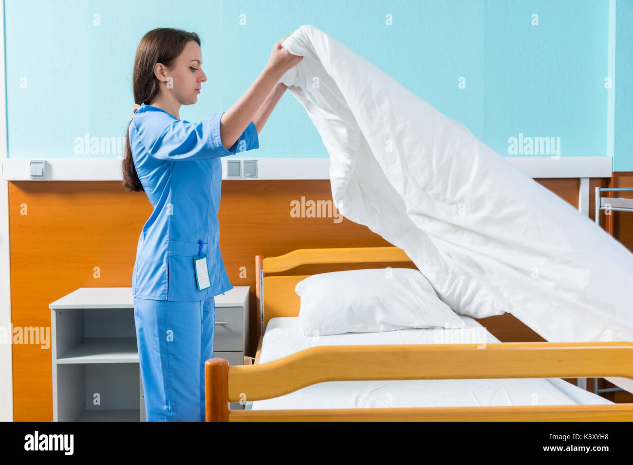 Young nurse in blue unifrom changing bedsheets of hospital bed in the ...