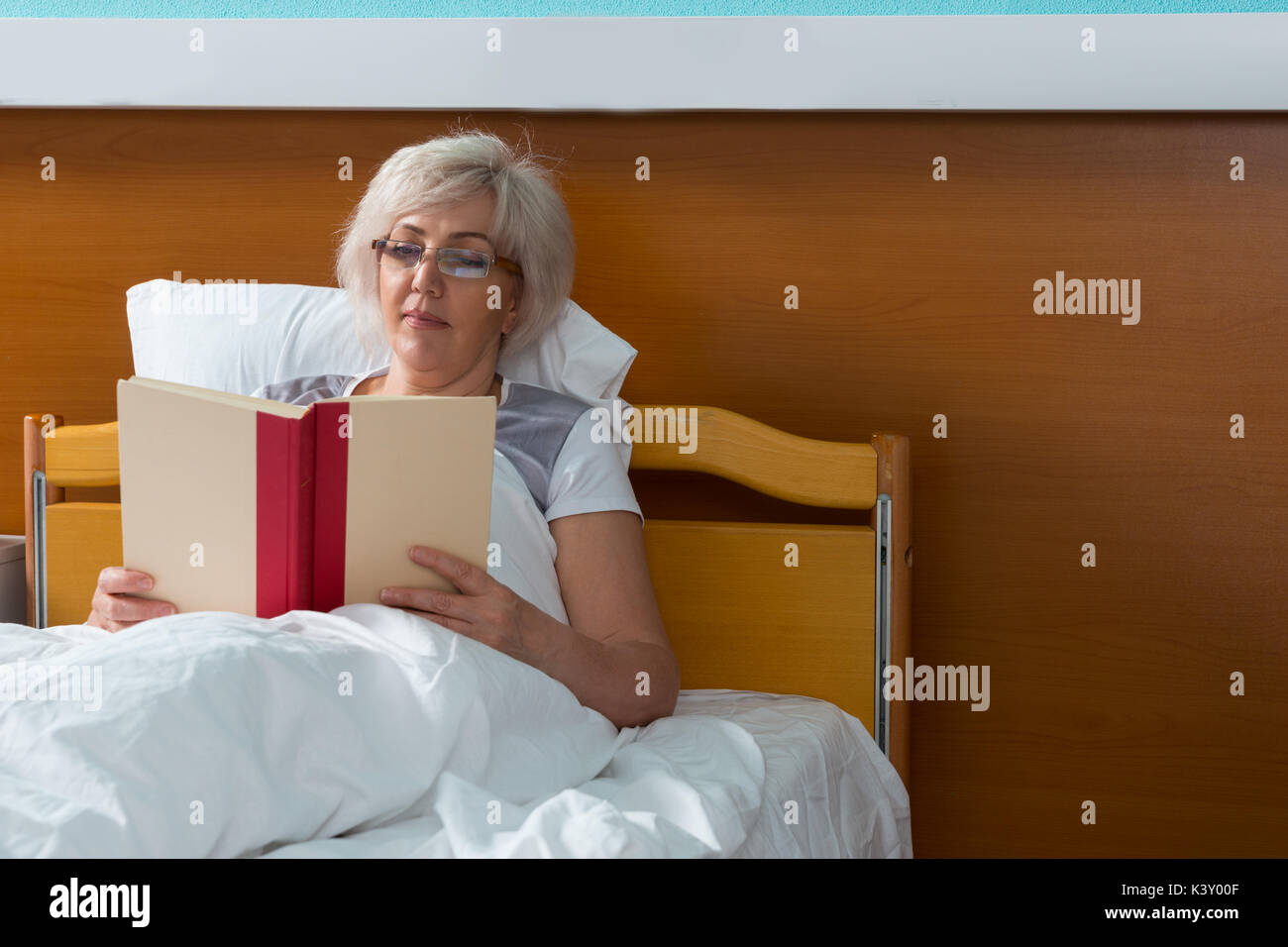 Female patient is reading a book, while lying in the hospital bed in ...