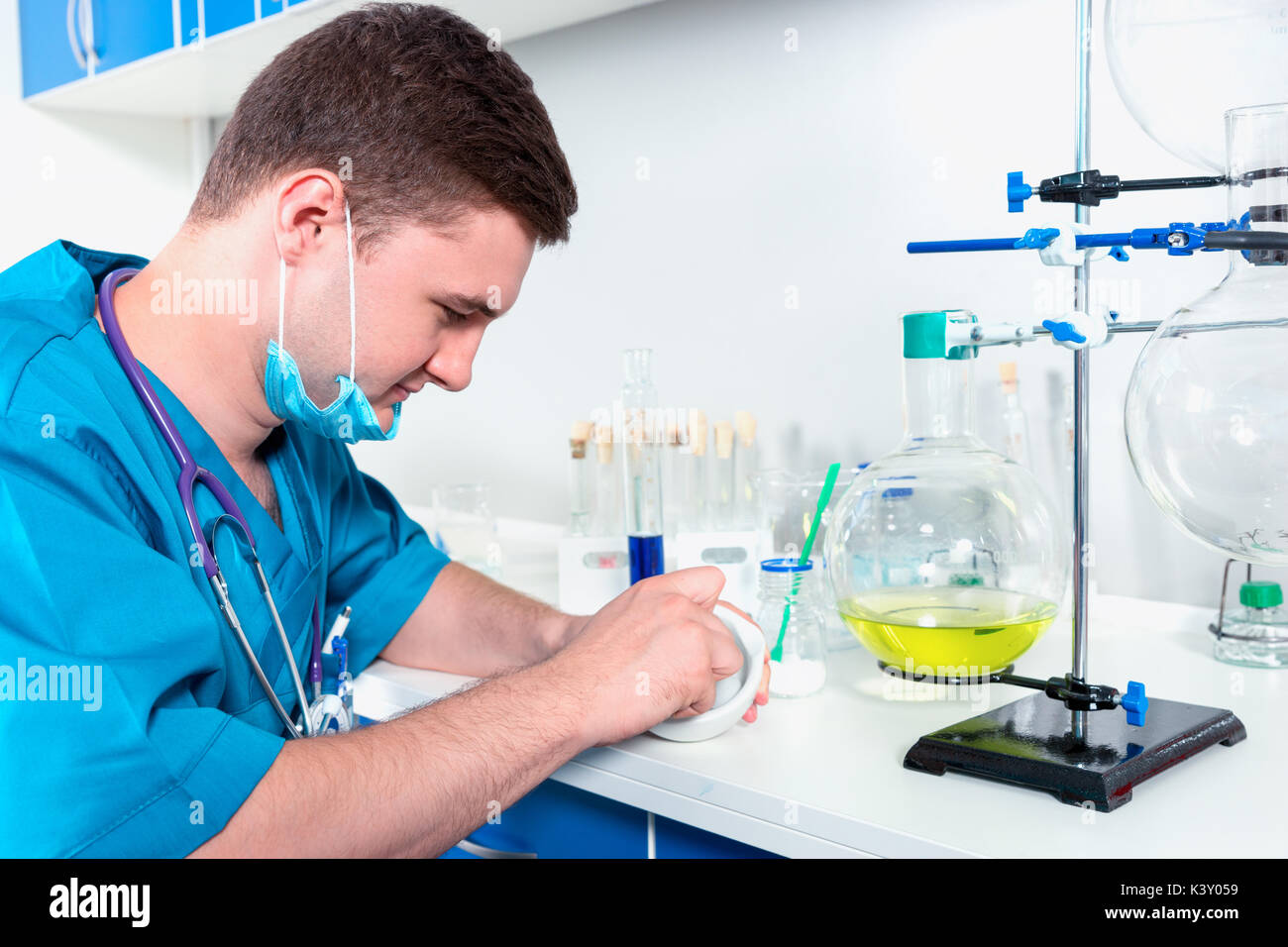 Male scientist in uniform wearing a mask preparing powder on ceramic ...