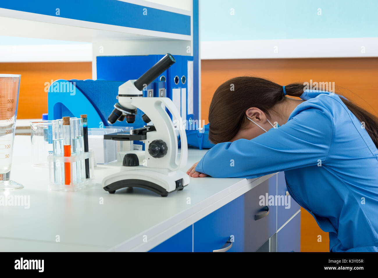 Tired female scientist in uniform is sleaping near her workplace with ...
