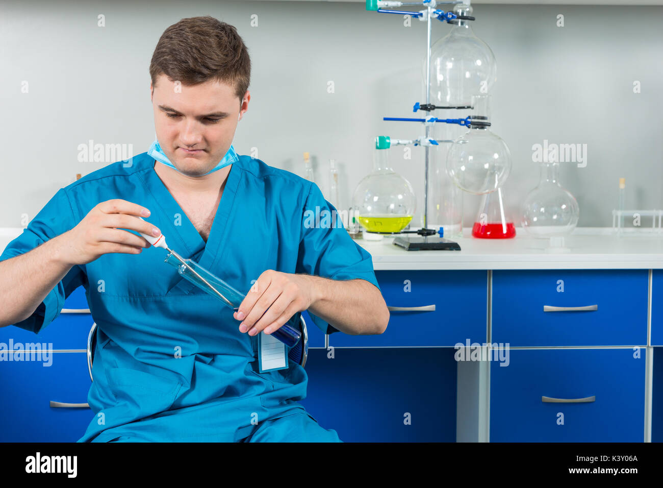 Young male scientist in uniform measures temperature of blue liquid in ...