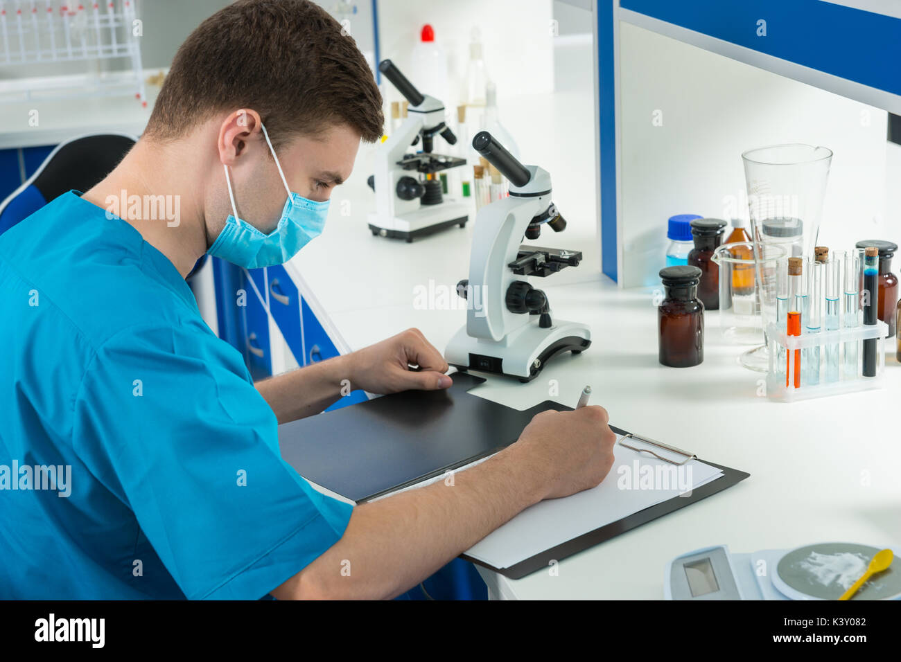 Scientist looking through microscope writing hi-res stock photography ...