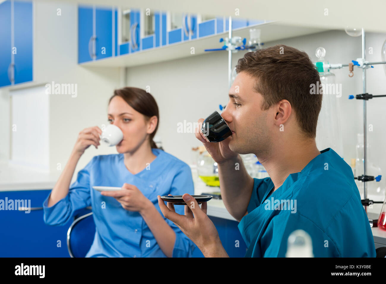 Two young scientists in uniform drinking a coffee after some research ...