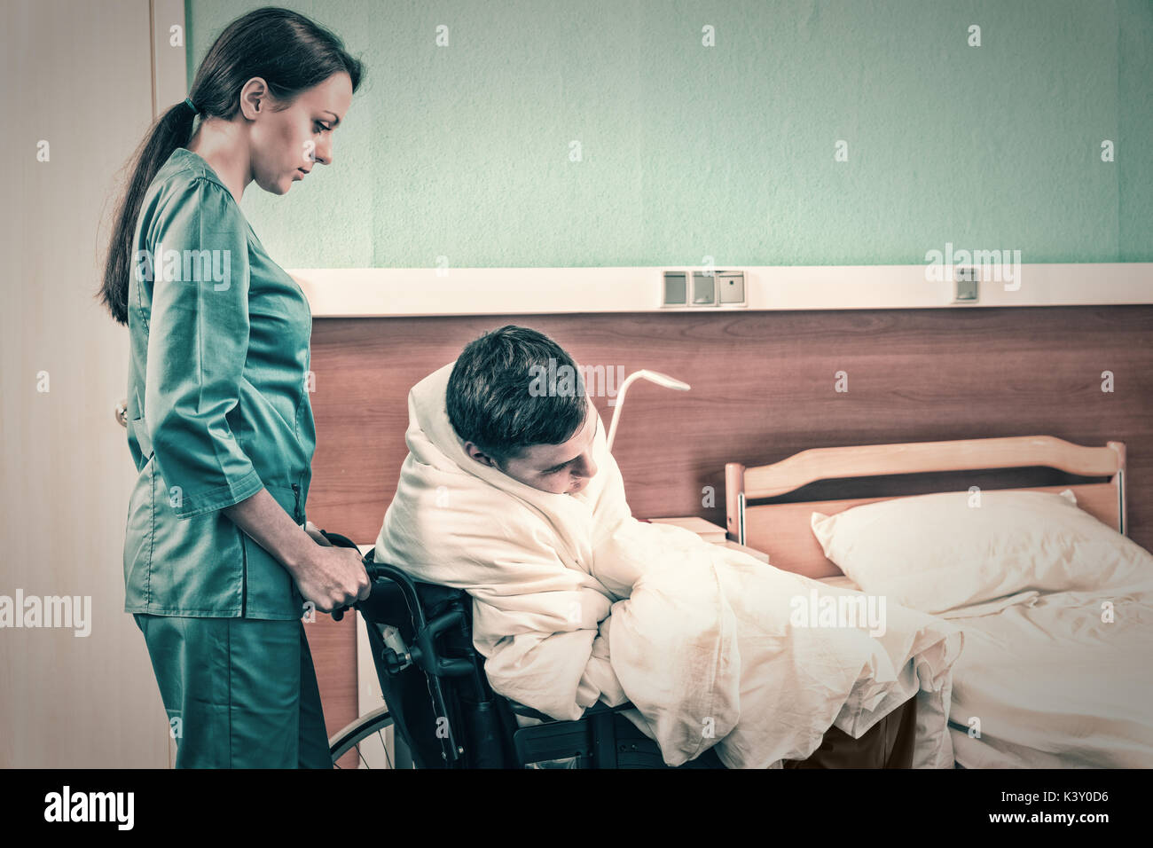 Attractive young nurse in uniform pulling wheelchair with ill patient ...