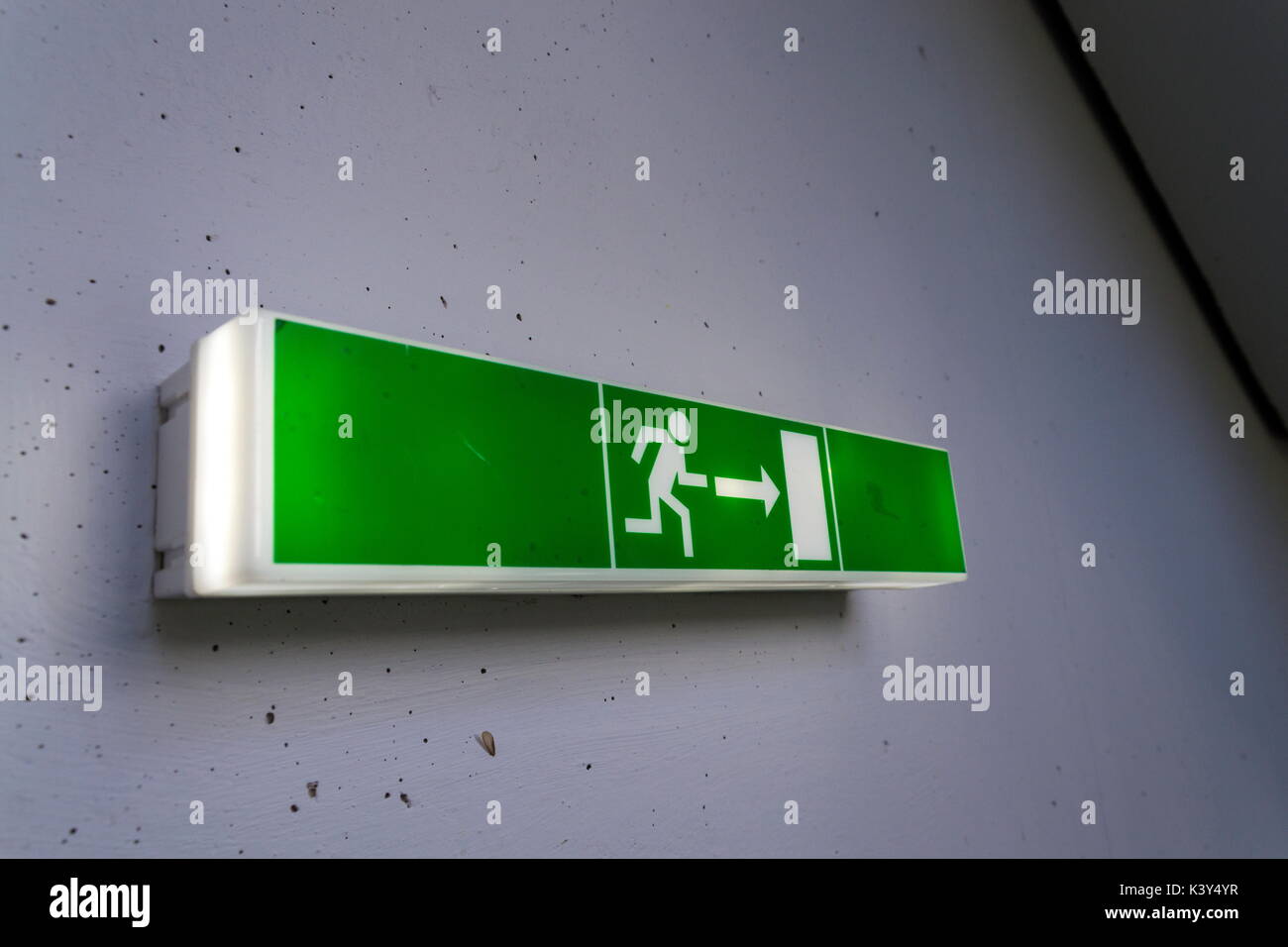 Green shining escape exit sign on white concrete wall Stock Photo - Alamy