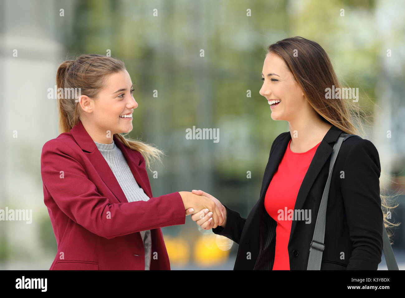 Side view of two happy executives meeting and handshaking on the street ...