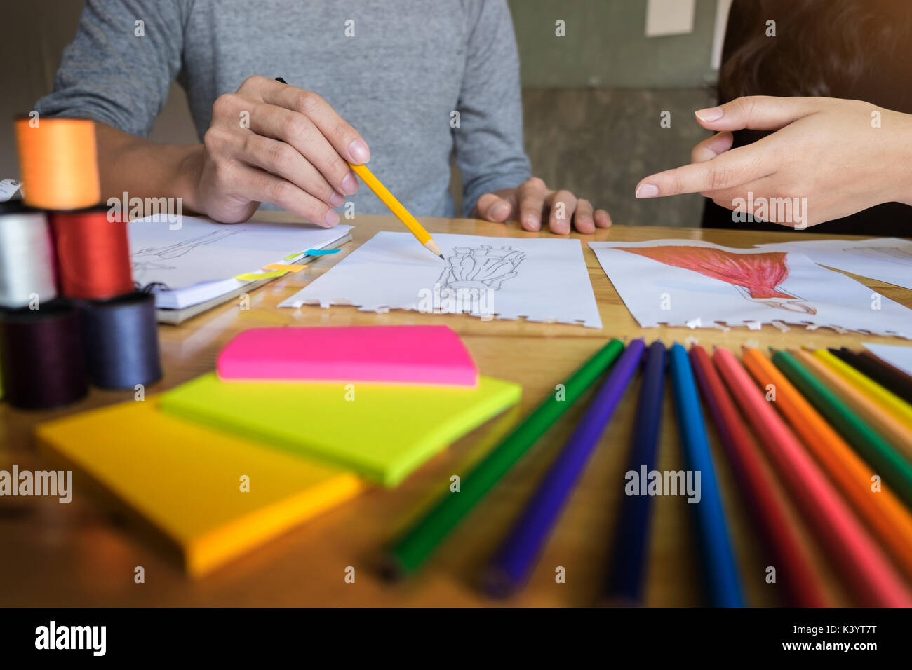 two young women working as fashion designers and drawing sketches and ...