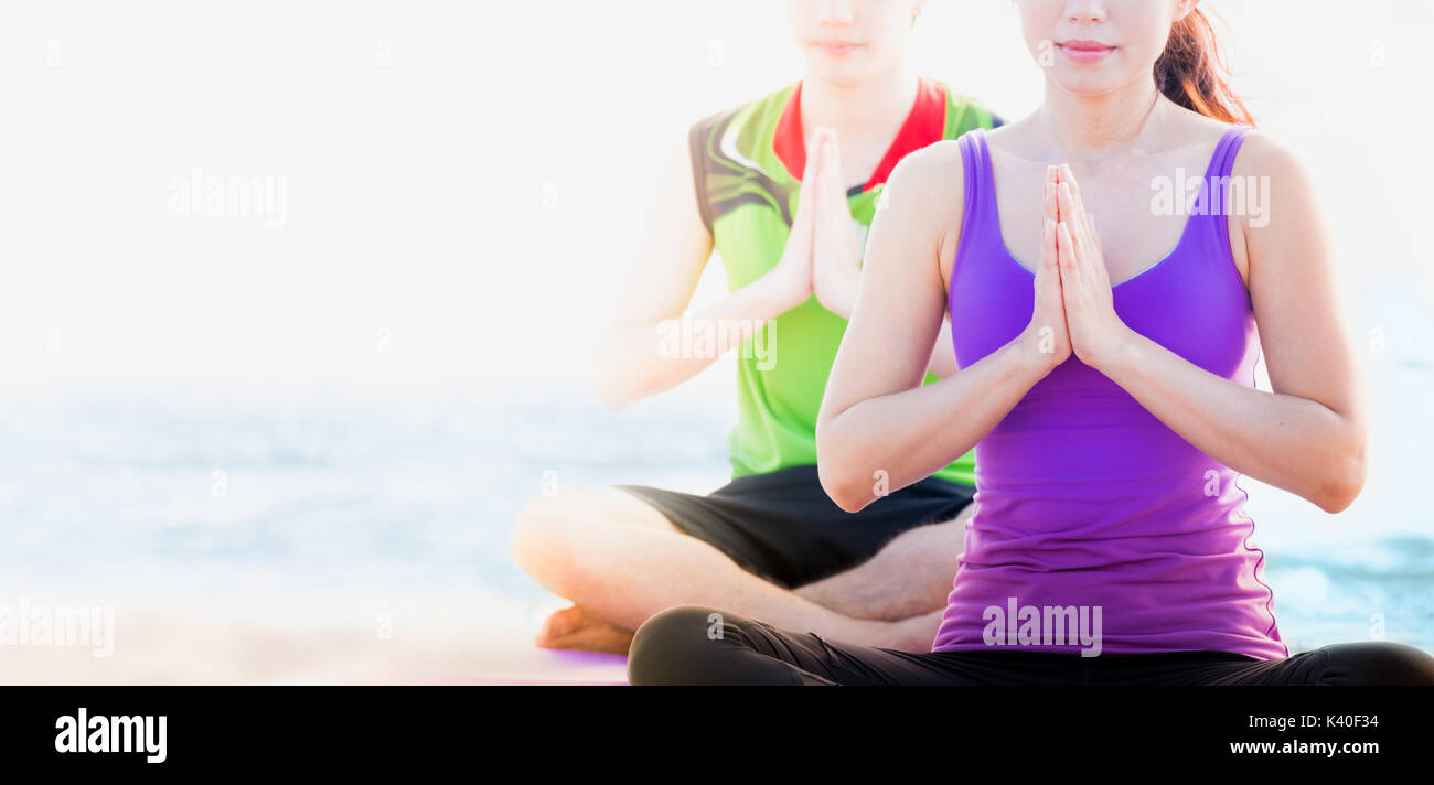 Close up female master yoga doing namaste pose with student at beach ...