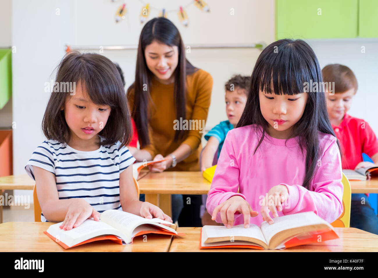 two Asian girl kid reading book in classroom and while teacher teach ...