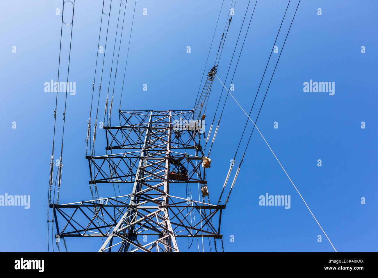 Electricians hanging high up suspended on electrical steel tower ...