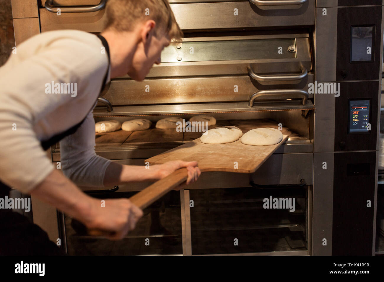 baker putting dough into bread oven at bakery Stock Photo - Alamy
