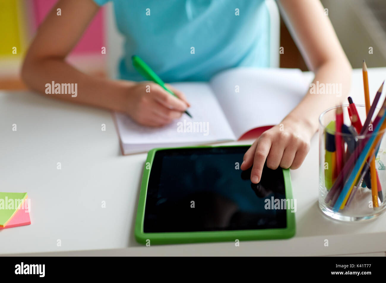 girl with tablet pc writing to notebook at home Stock Photo - Alamy