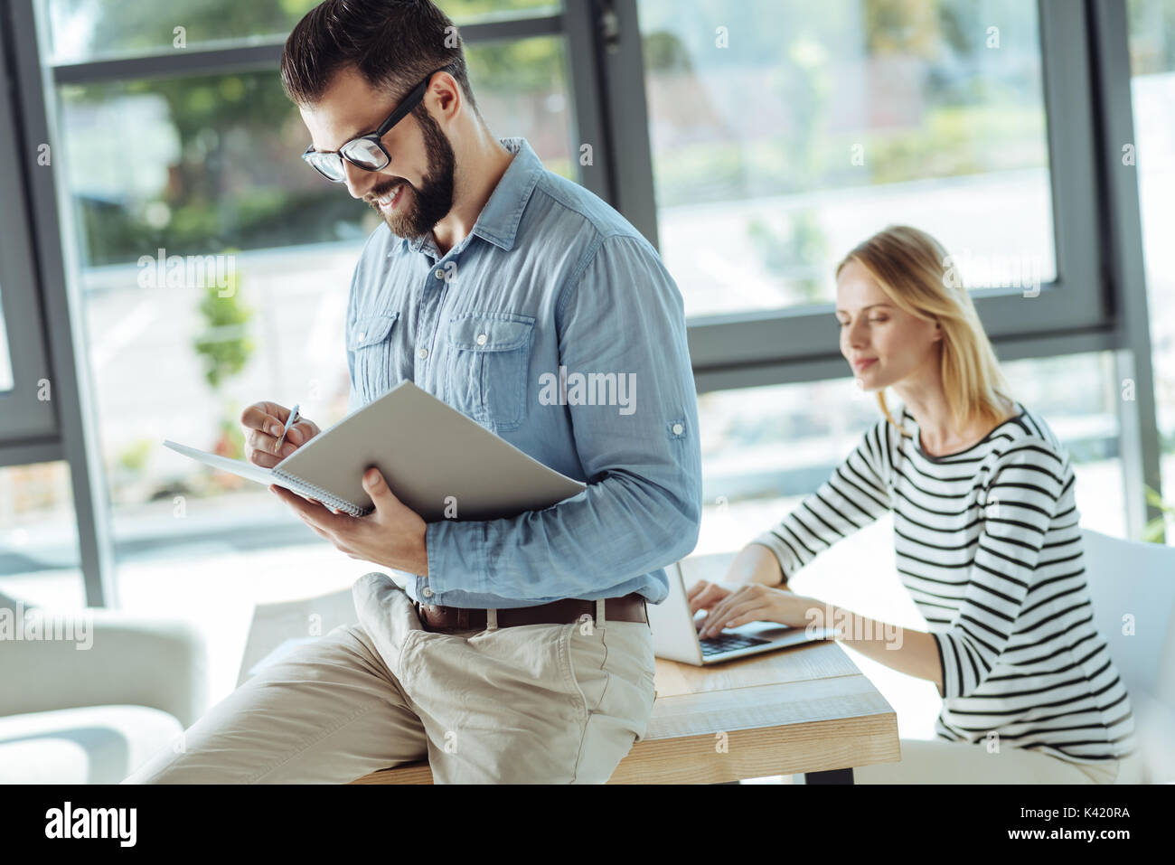 Smiling man writing in notebook while his colleague typing Stock Photo ...