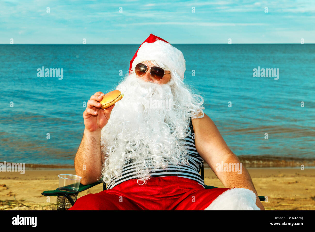 Santa Claus on the beach eating a hamburger. The concept of unhealthy ...