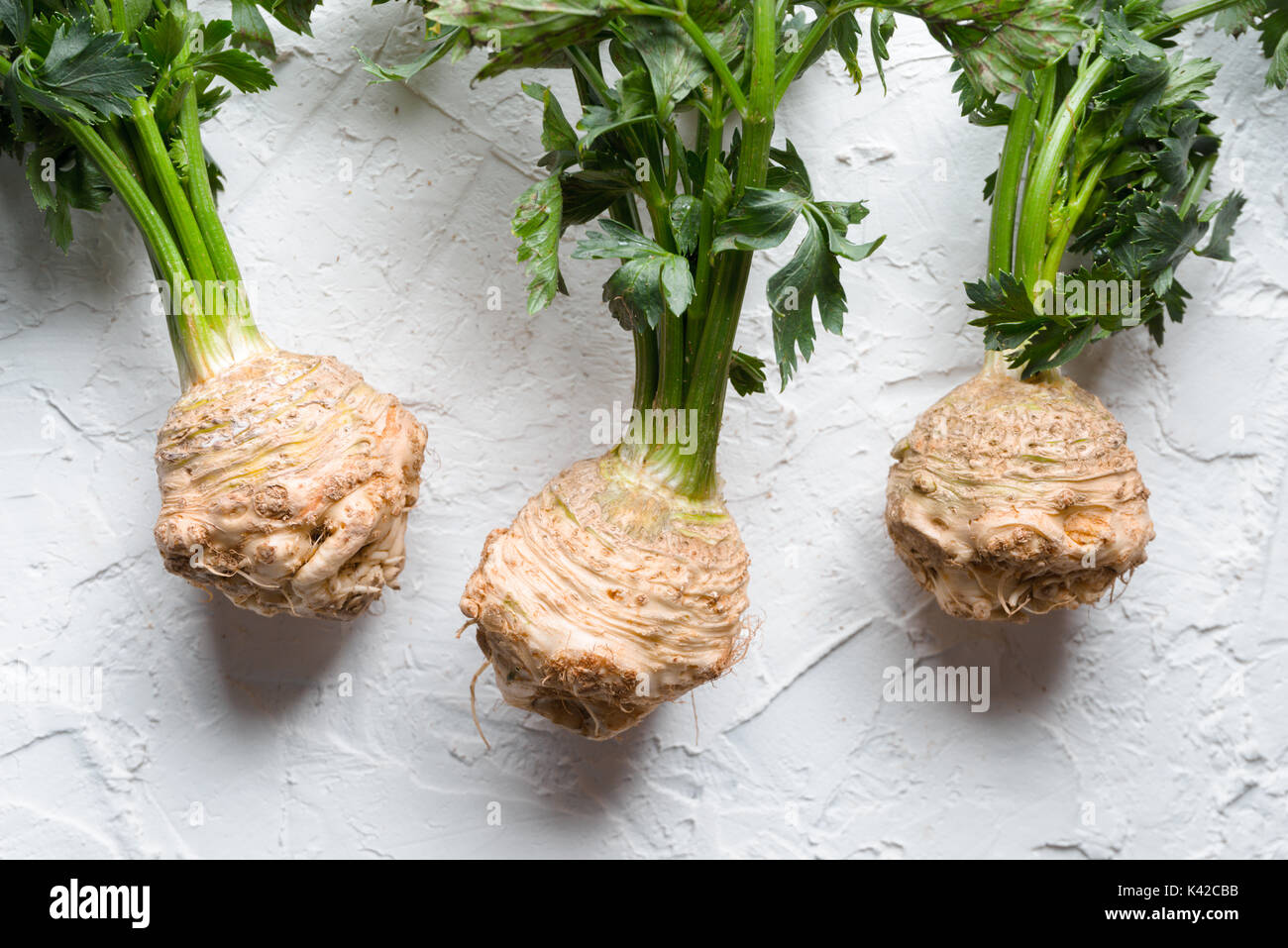 Celery roots with green leaves on a white table horizontal Stock Photo ...