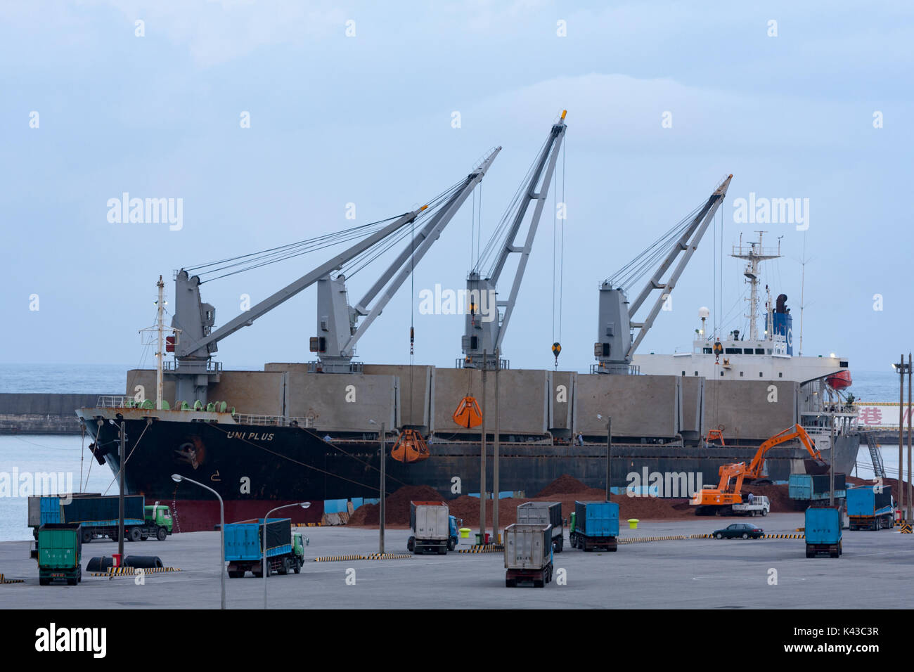 Uniplus bulk carrier cranes unloading loads with dump trucks waiting ...